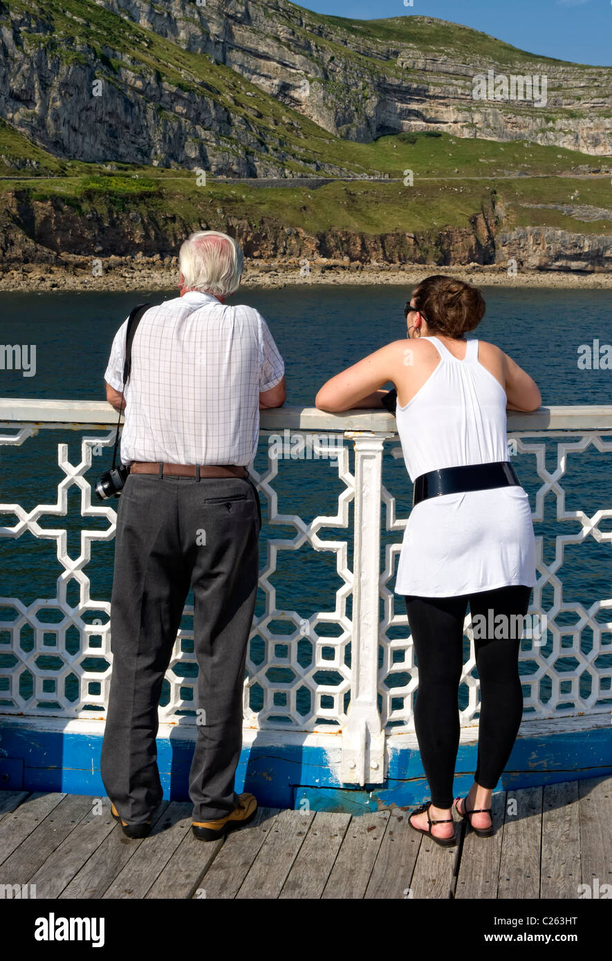 Man and woman leaning on the rail of Llandudno Pier and looking toward ...