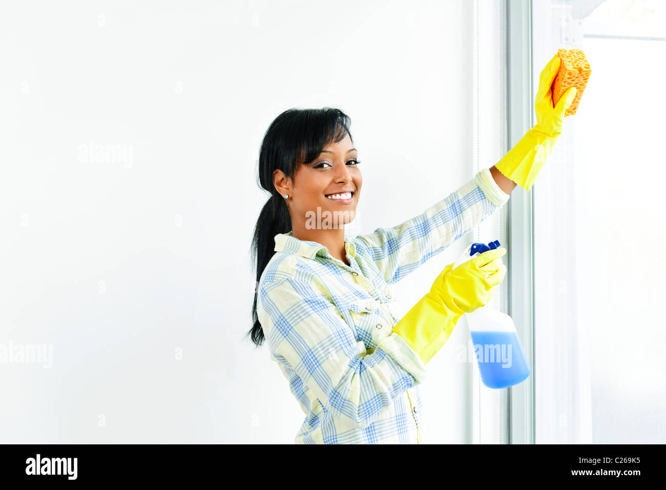 Smiling black woman cleaning windows with glass cleaner Stock Photo - Alamy