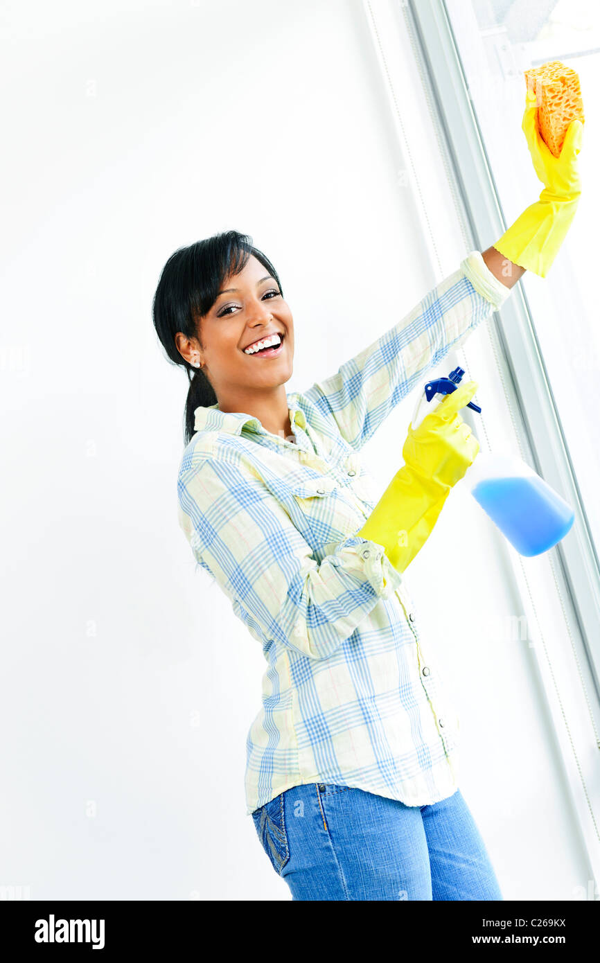 Smiling black woman cleaning windows with glass cleaner Stock Photo - Alamy
