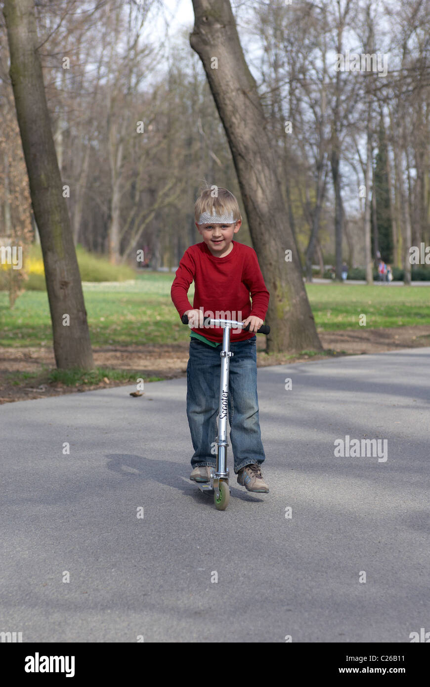 A young child blond boy on a scooter in park with injured head ...