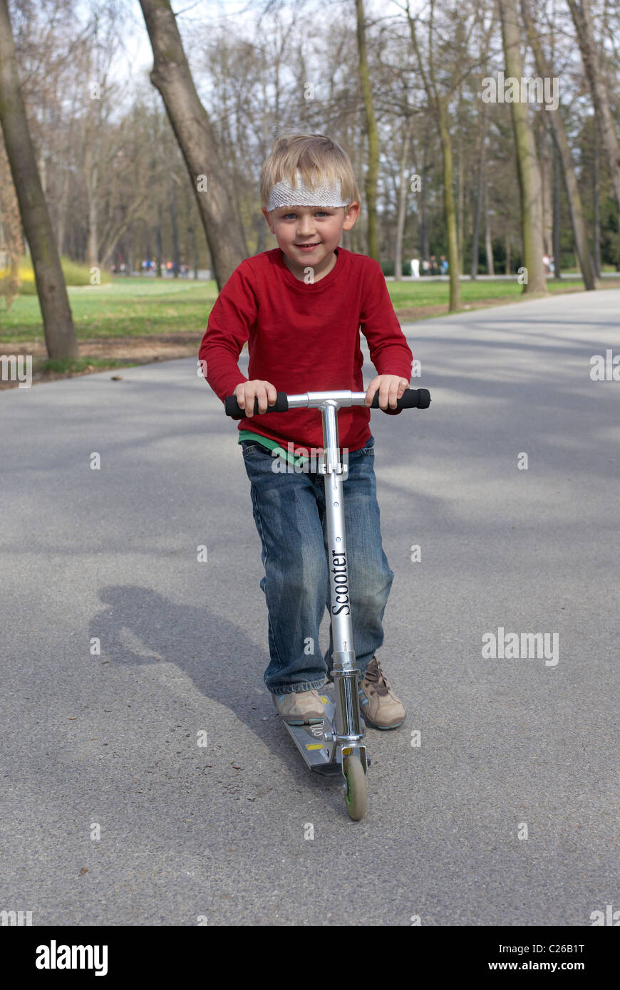 A young child blond boy on a scooter in park with injured head ...