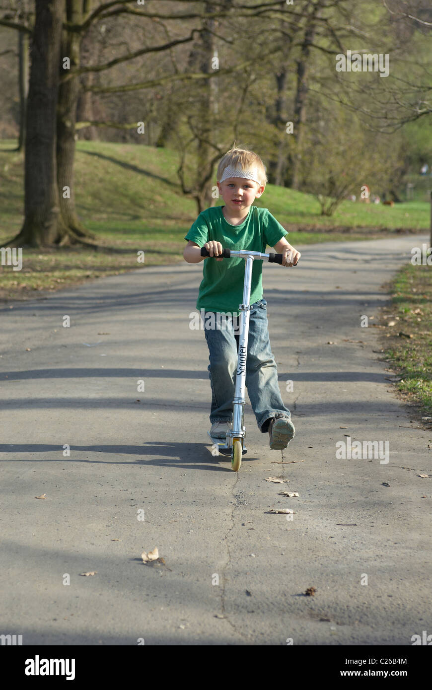 A young child blond boy on a scooter in park with injured head ...