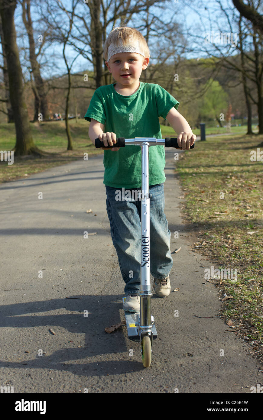 A young child blond boy on a scooter in park with injured head ...