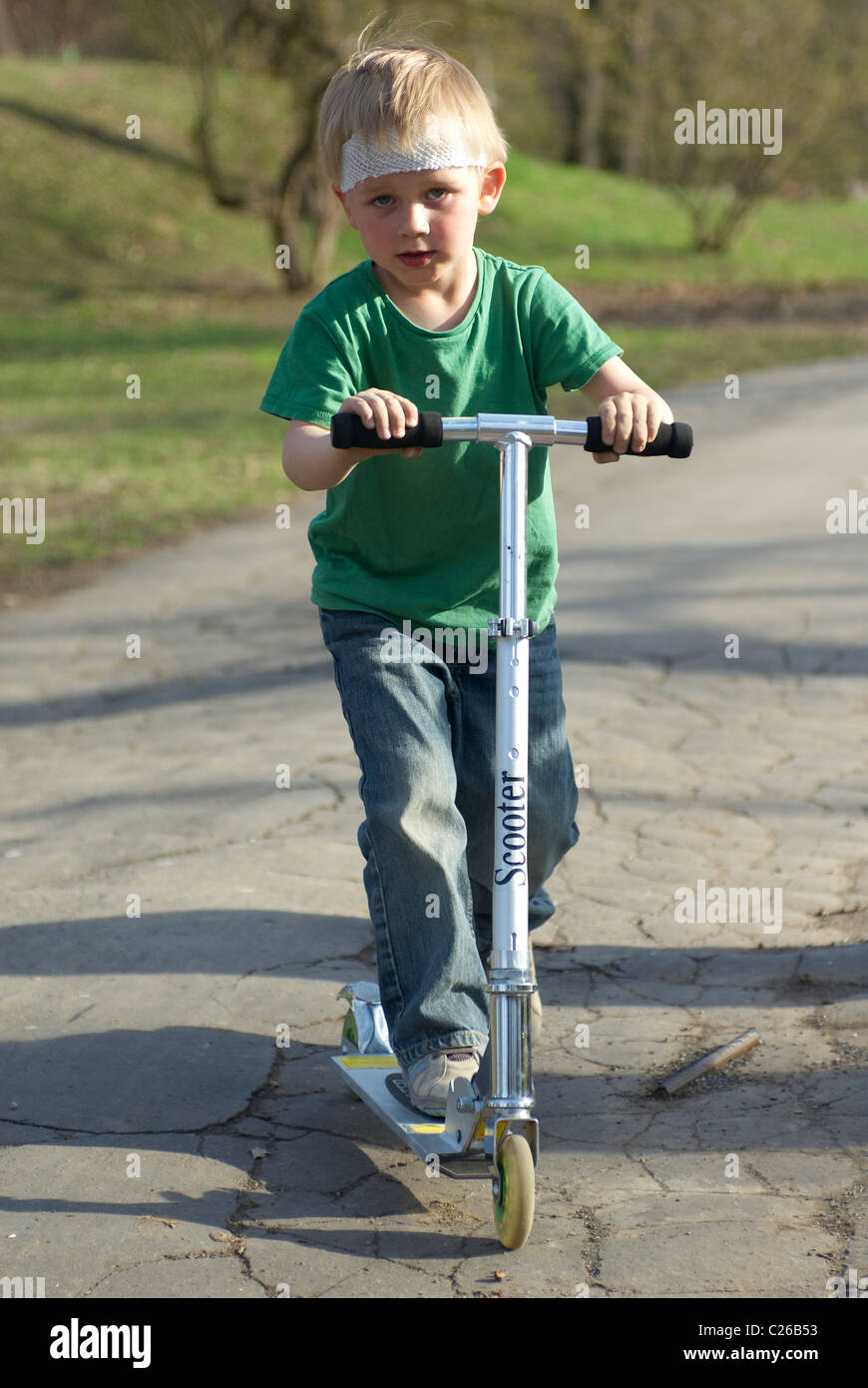 A young child blond boy on a scooter in park with injured head ...