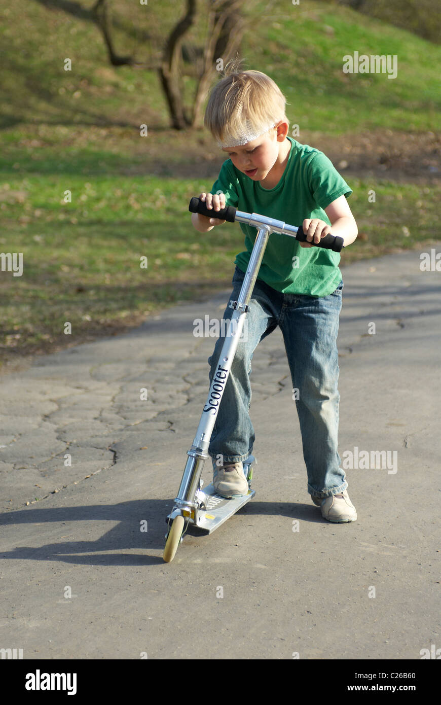 A young child blond boy on a scooter in park with injured head ...