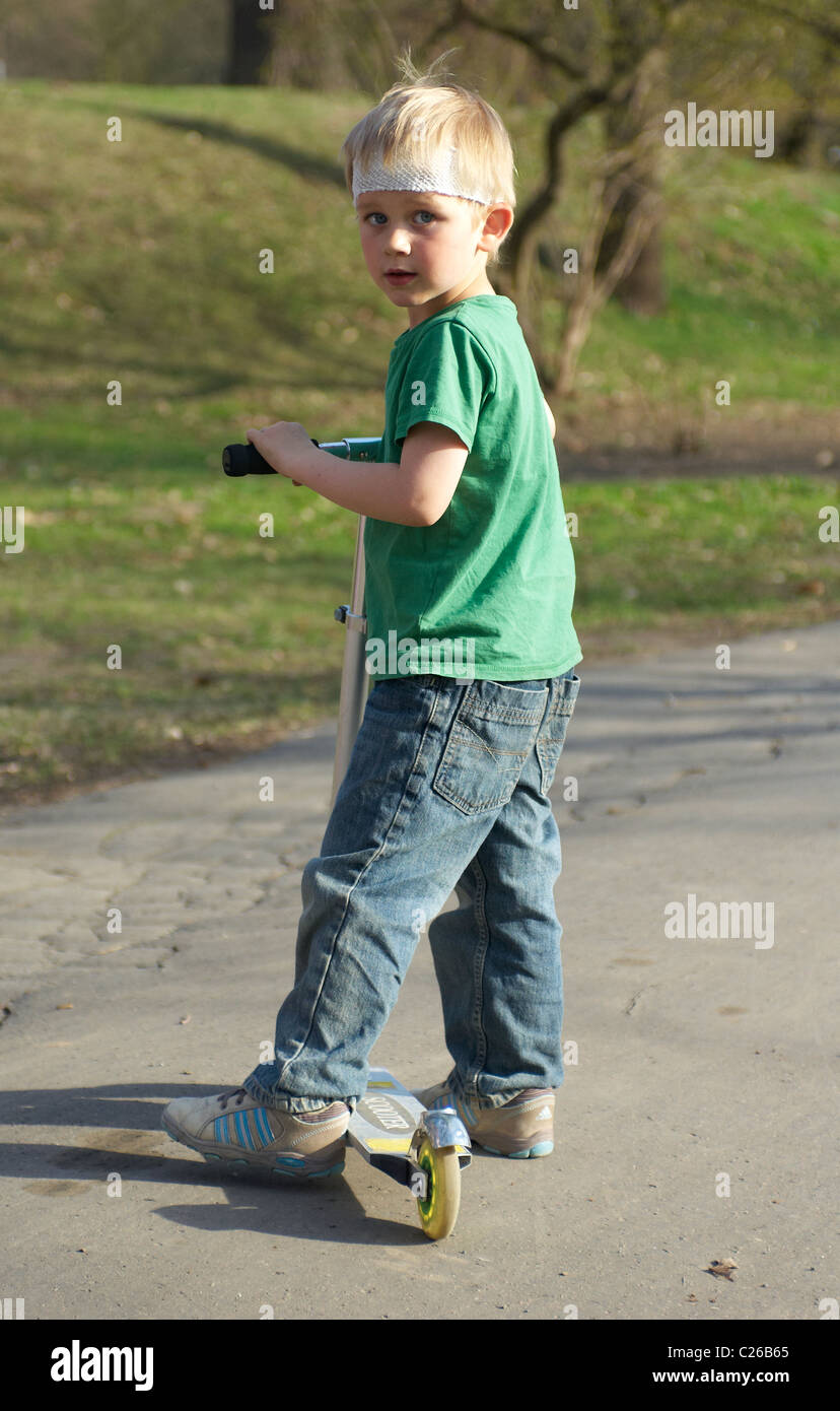 A young child blond boy on a scooter in park with injured head ...