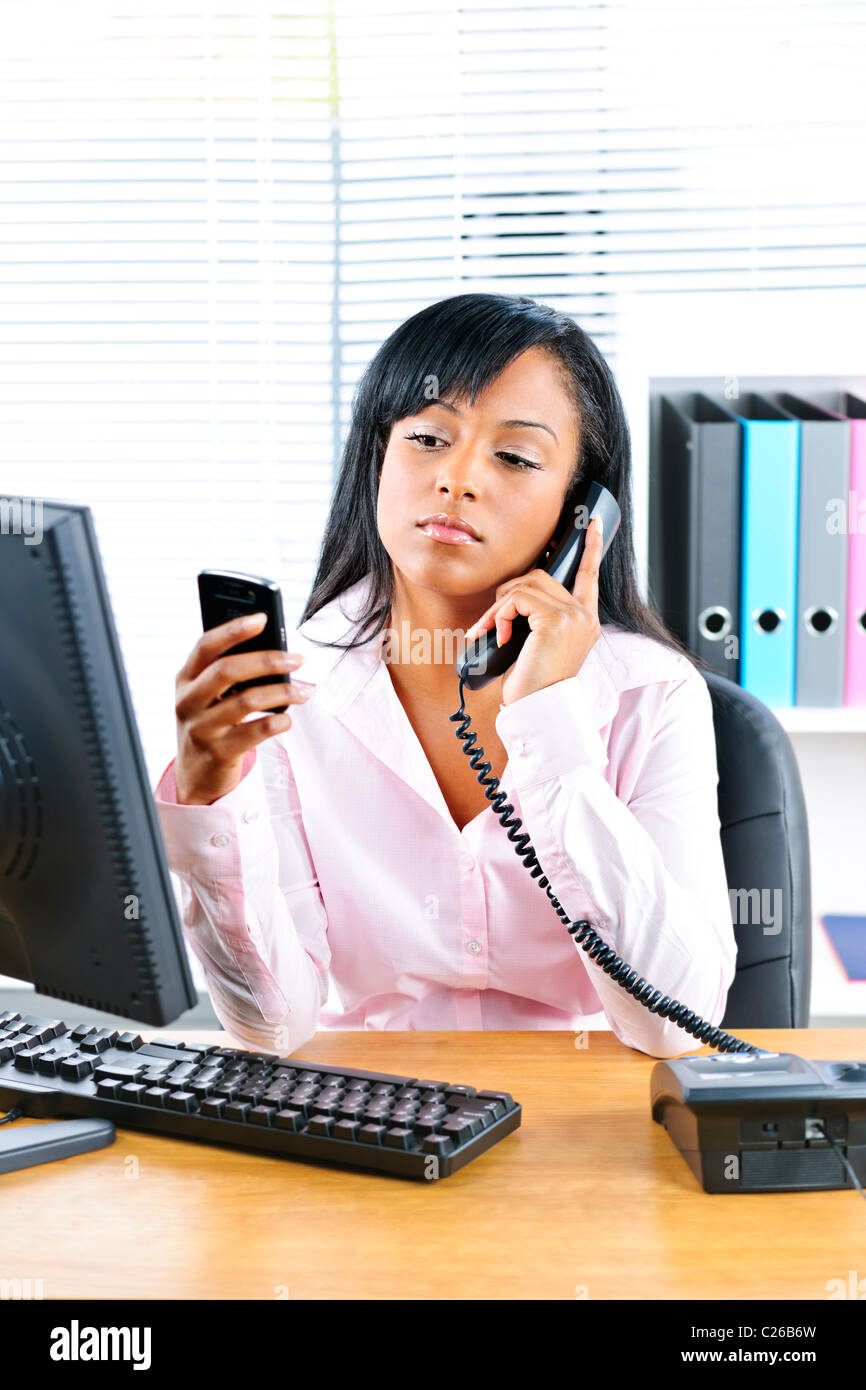 Young black business woman multitasking using two phones in office ...