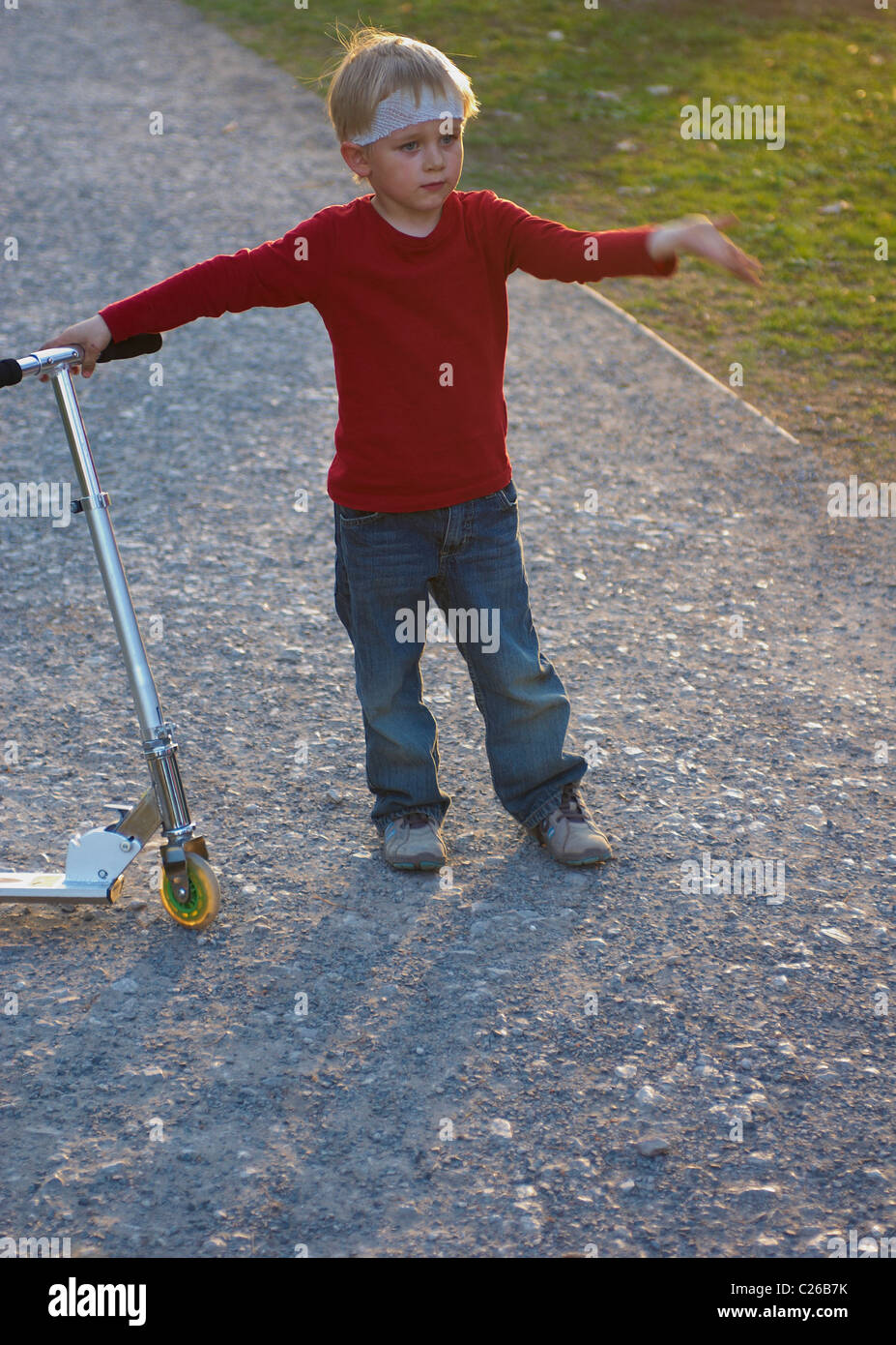 A young child blond boy on a scooter in park with injured head ...