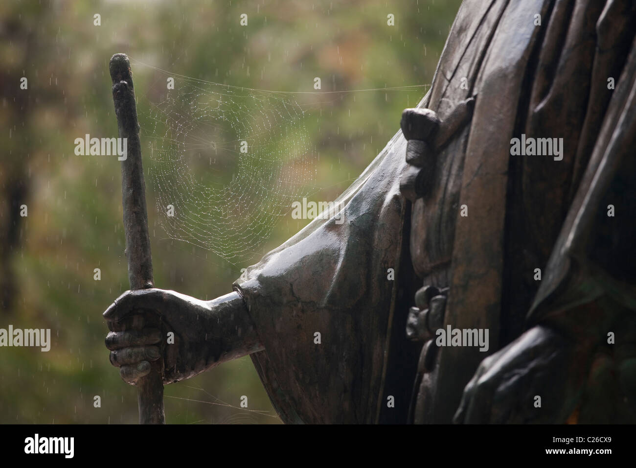 Closeup of statue with walking stick and spider web with raindrops at ...