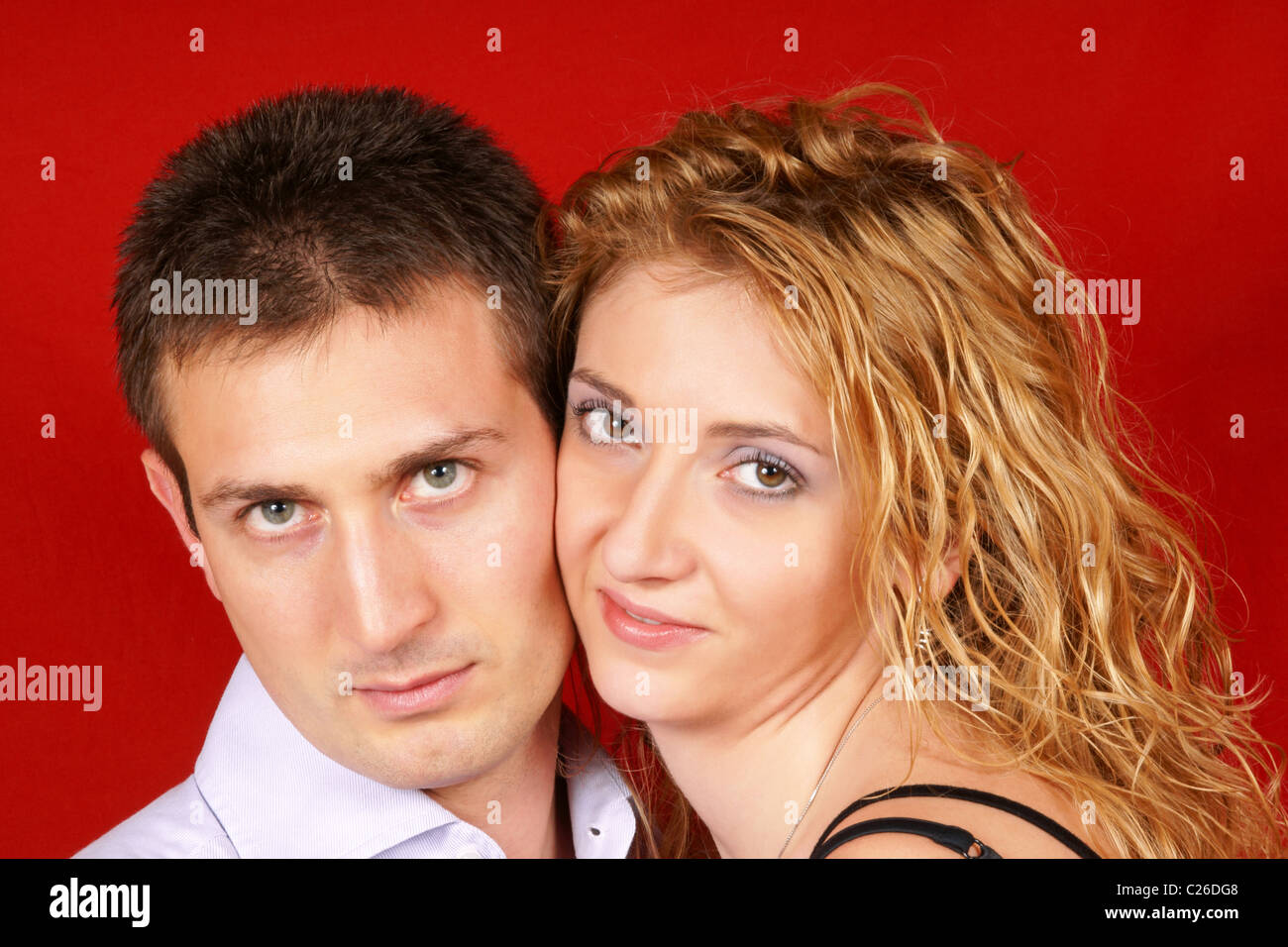 Beautiful young couple in love looking at camera over a red background ...