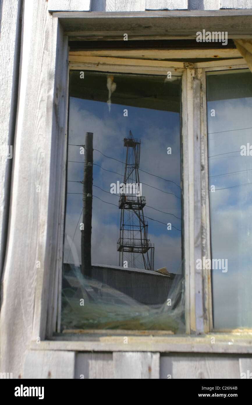 Derrick is reflected in a broken window of wooden shack. Yamal ...