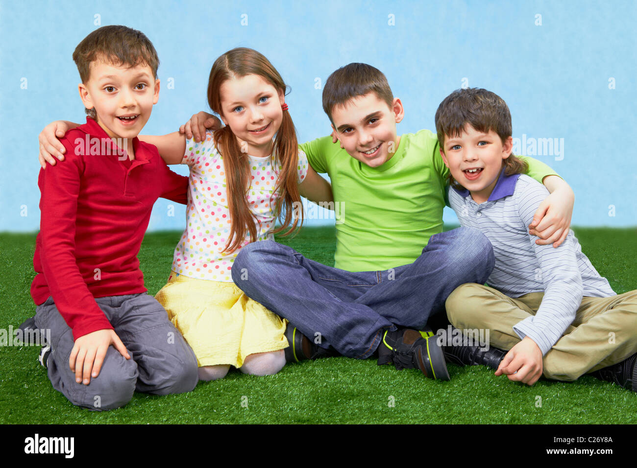 Group of four children sitting on a green grass Stock Photo - Alamy