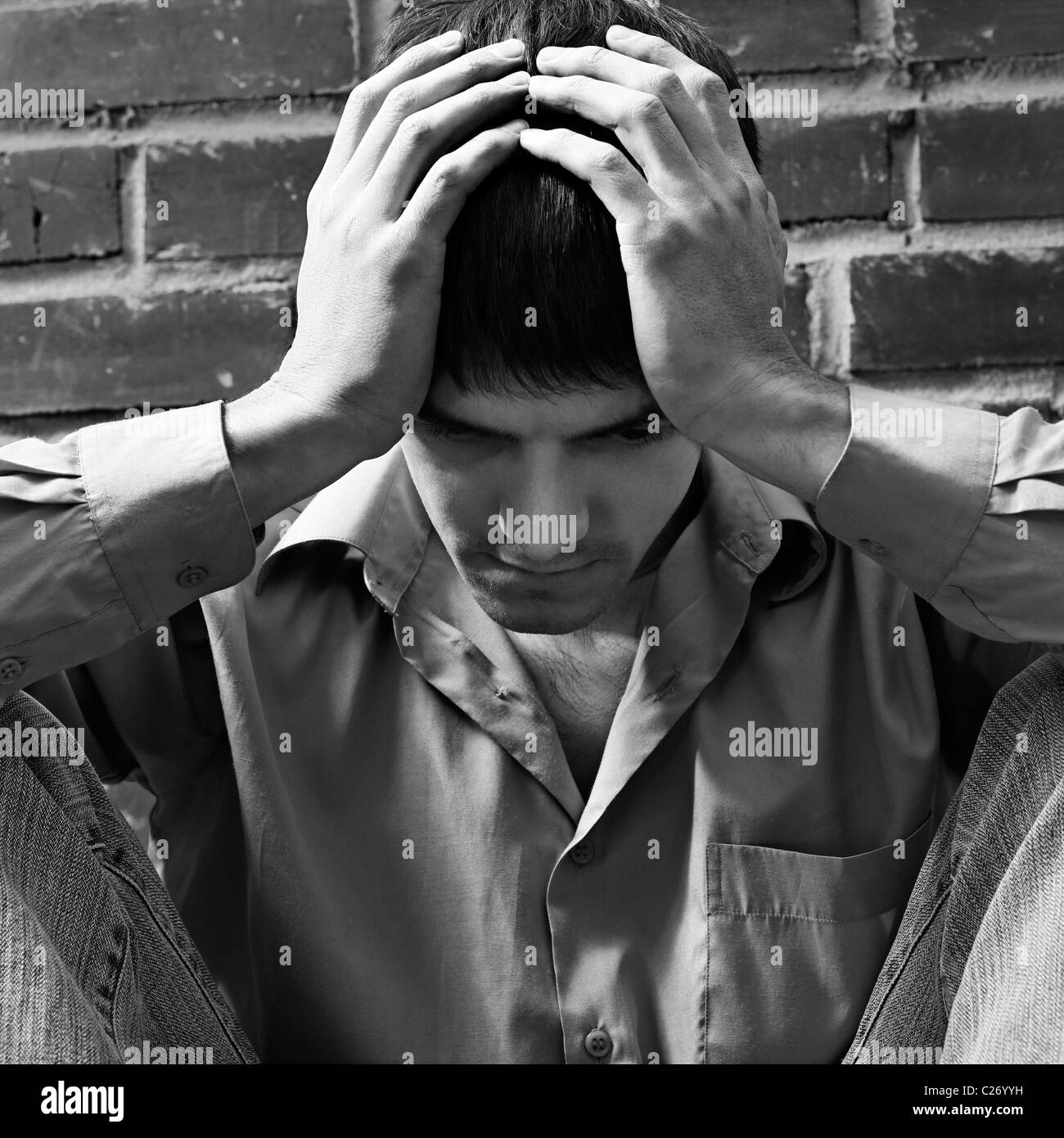portrait of young brunet guy in depression sitting near red brick wall ...