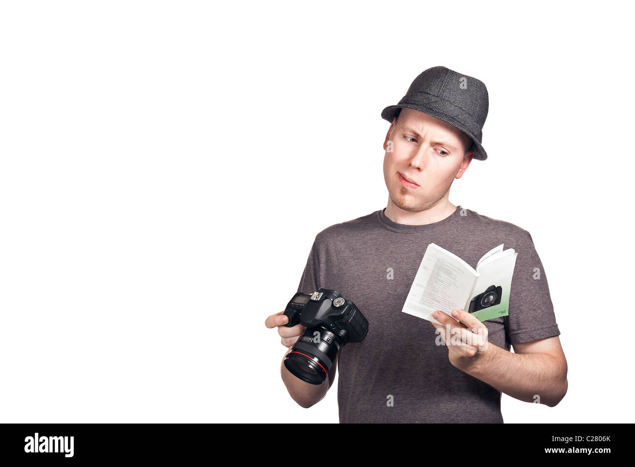 A young man looking confused reading an instruction manual for a DSLR ...