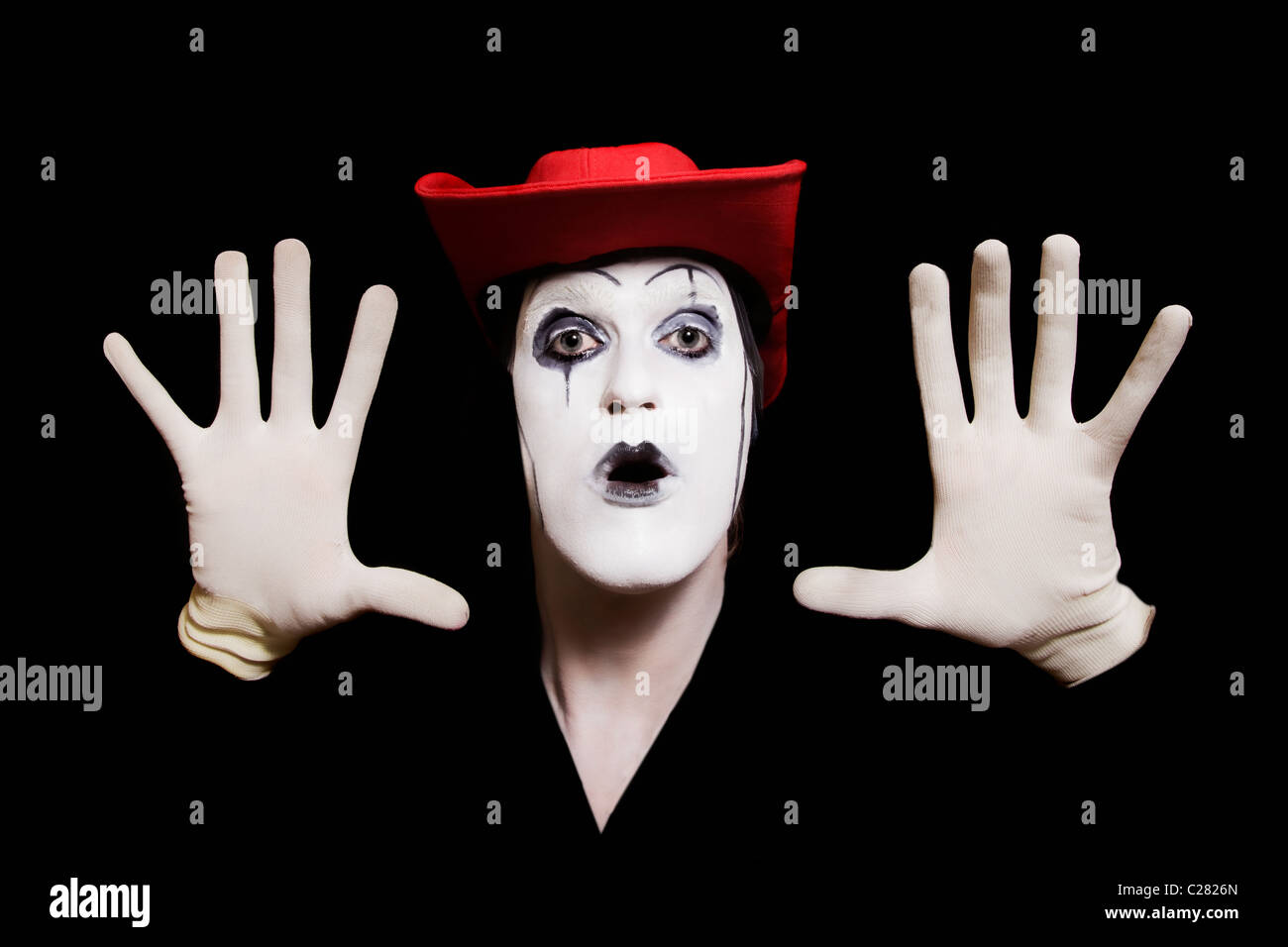 face and hands of mime with dark make-up in red hat on black background ...