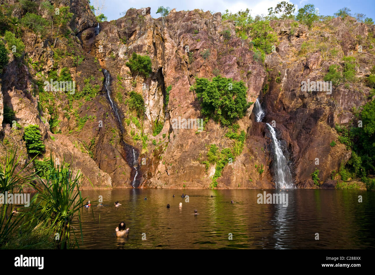 A waterfall cascades down a cliff face into a cool swimming waterhole ...