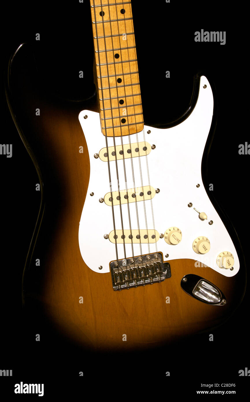 A sunburst colored electric guitar emerges from a black background ...