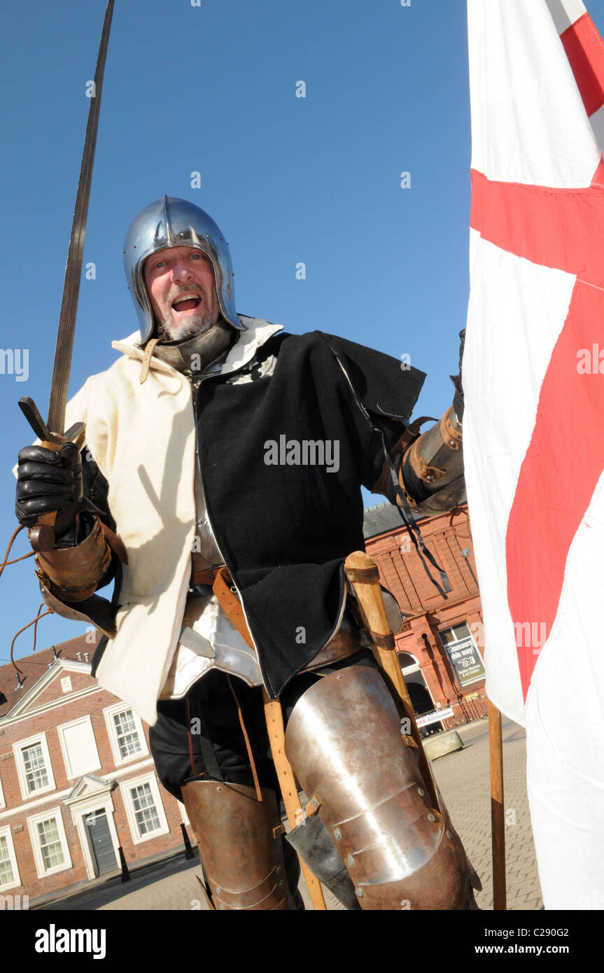 Man dressed as a English knight holding a sword and large flag of St ...