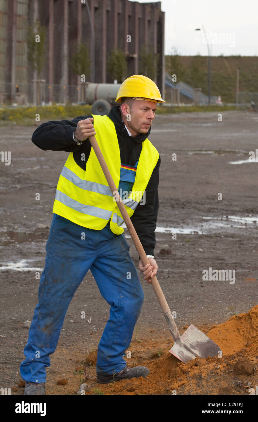 Construction worker in workwear and in yellow hardhat digging sand with ...