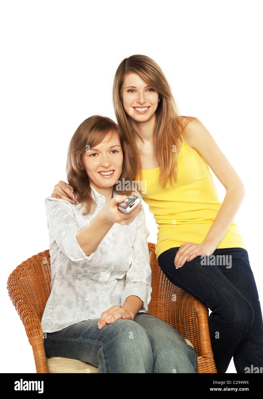 Two smiling pretty blond girls watch TV; isolated on white background ...