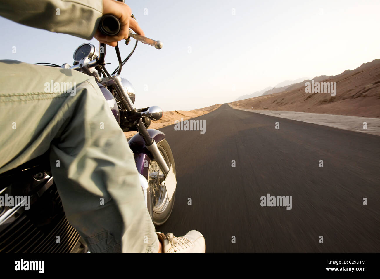 Road level view of custom motorcycle riding down a desert road at ...