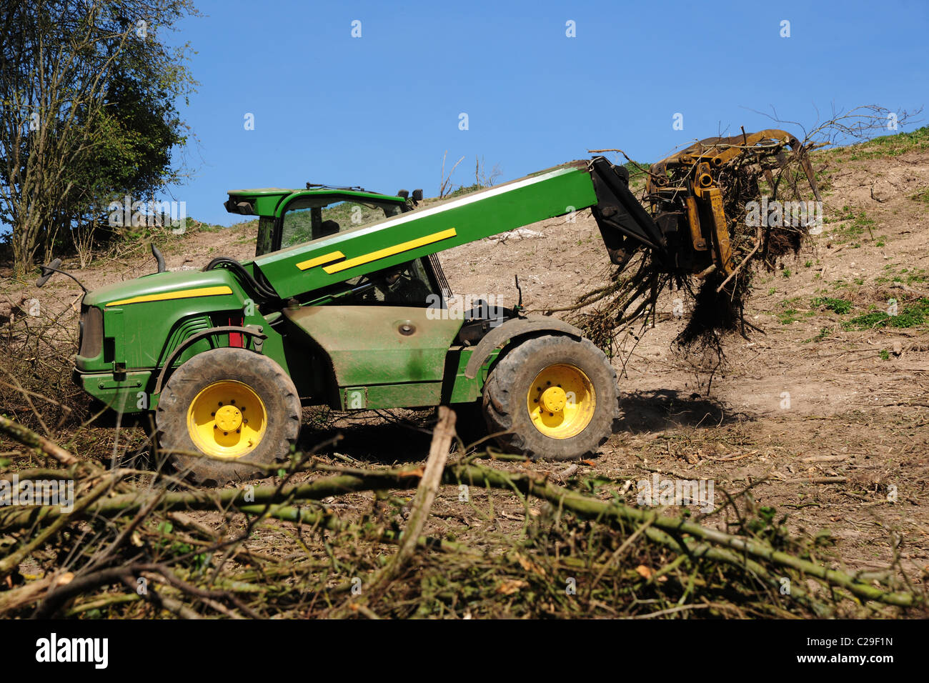 A farmer uses a tractor to clear hedgerows ready for planting out crops ...