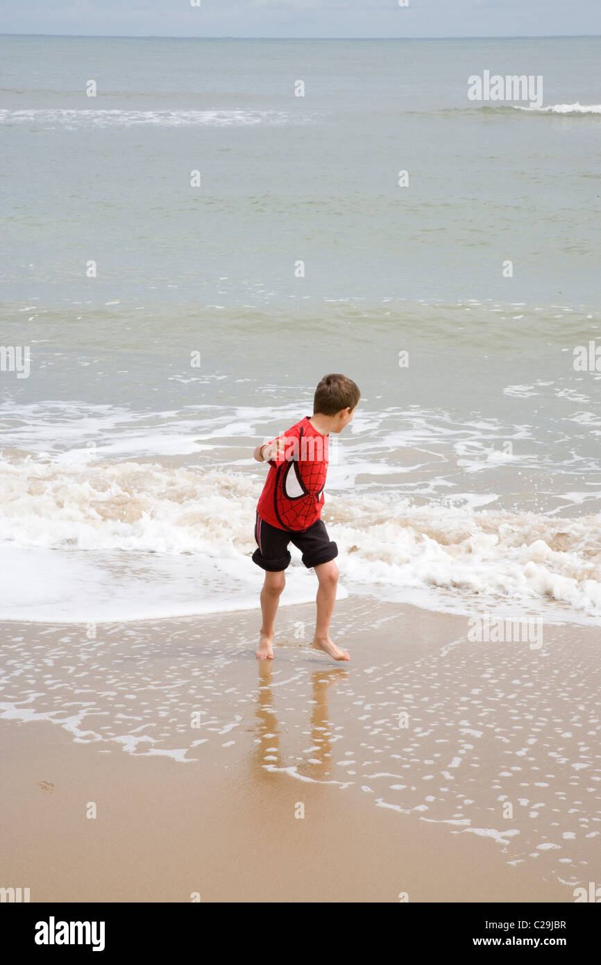 Boy playing on the sea shore evading incoming tidal waves. Sea Palling ...