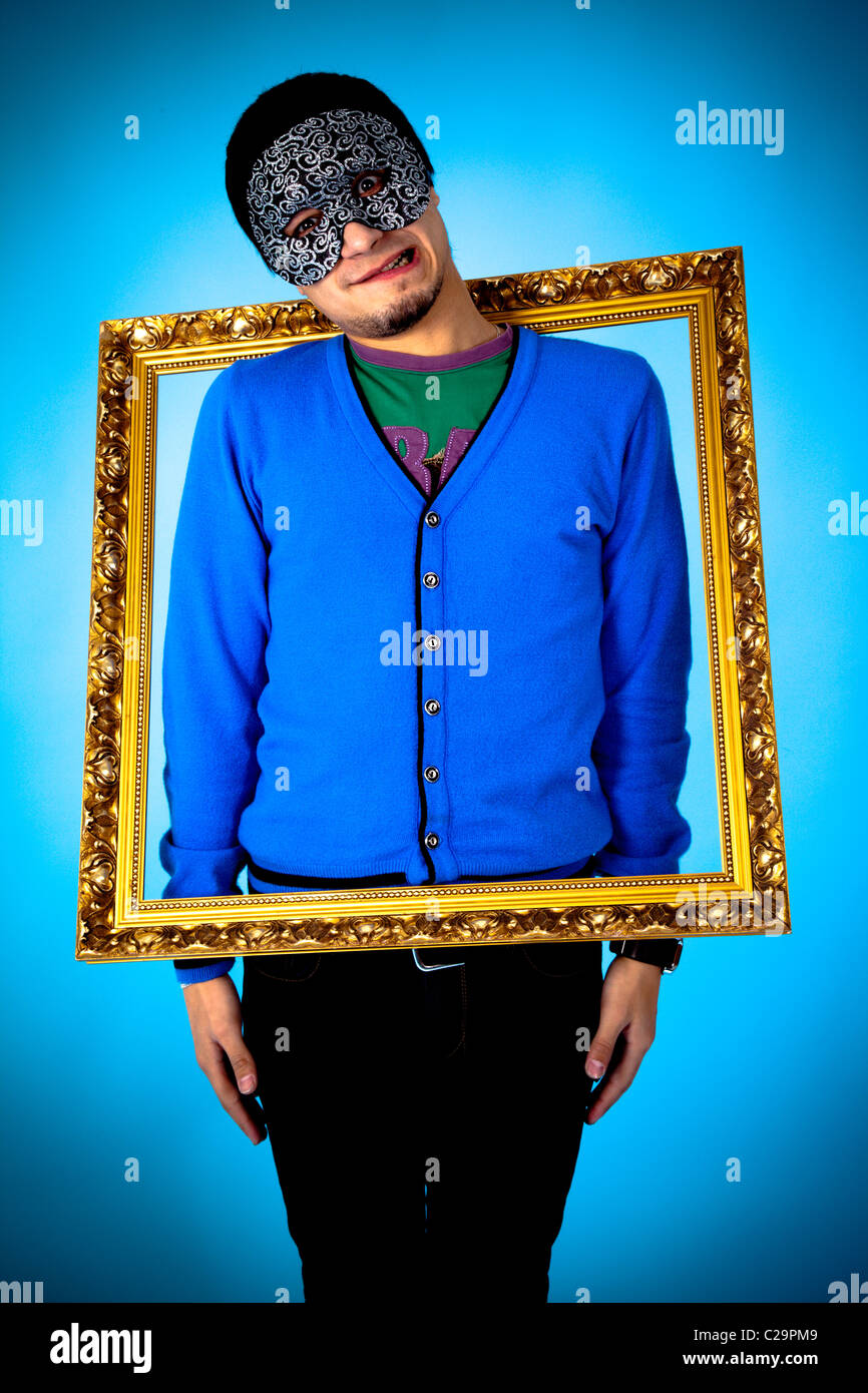 Young funny man with gold frame standing on the blue background Stock ...