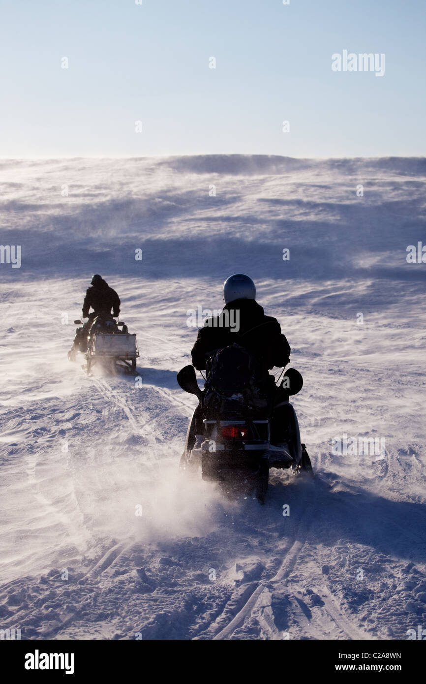 Two people riding up a hill on snowmobiles Stock Photo - Alamy