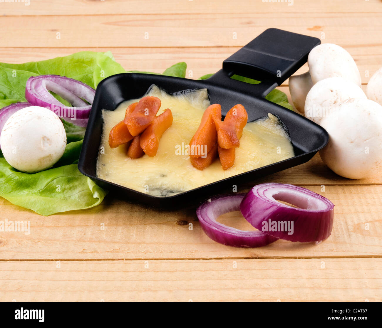 Raclette pan with cheese and cocktail sausages on wooden background ...