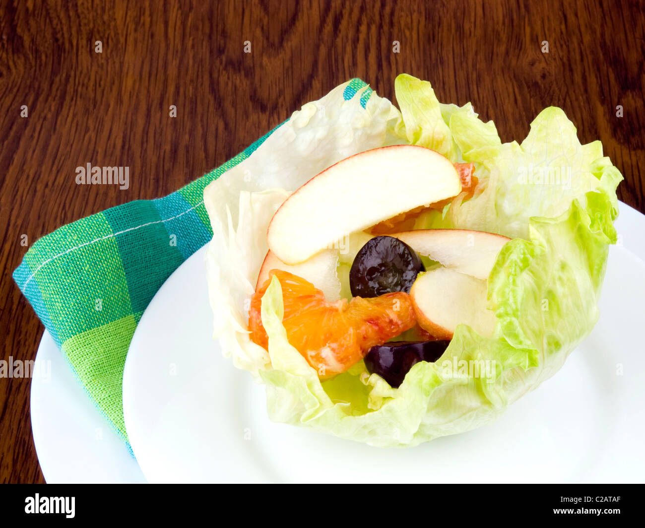 Sliced apple, orange and grapes in iceberg lettuce leaf on white plate ...