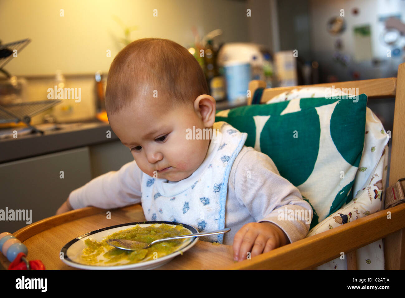 Baby girl contemplating food and spoon Stock Photo - Alamy