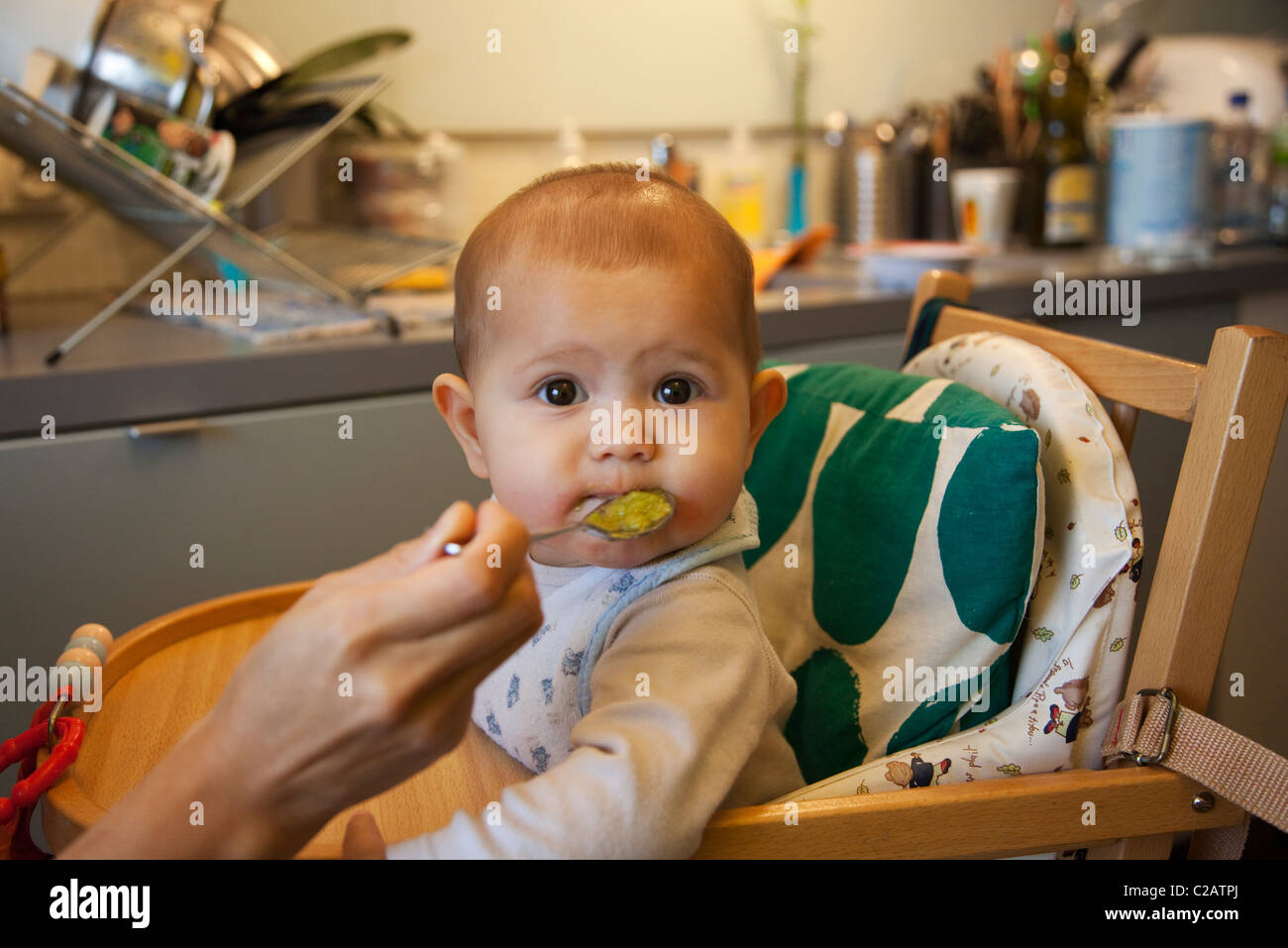Baby girl being fed in high chair Stock Photo - Alamy