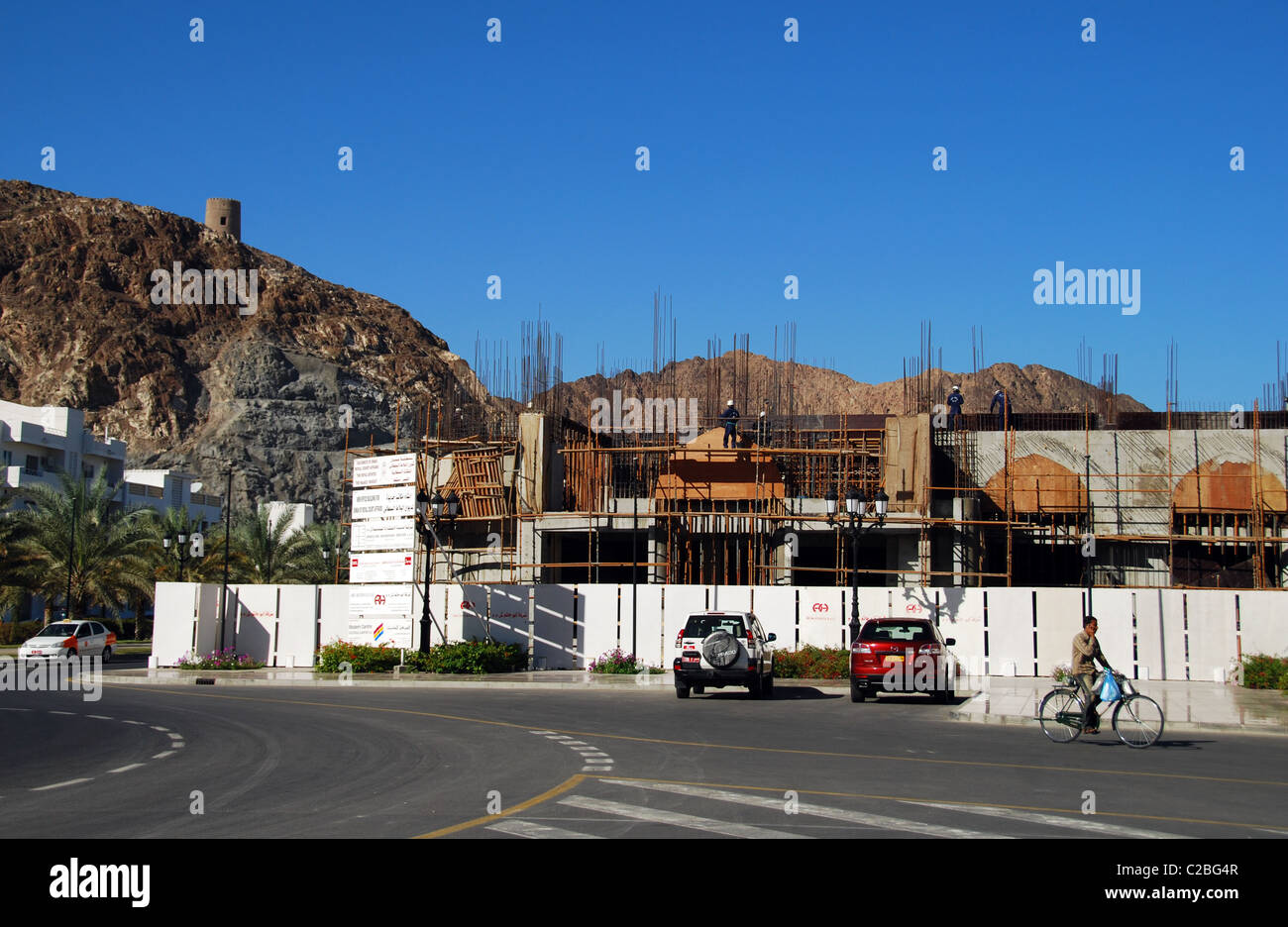 Oman, Muscat, man cycling on the road by a building under construction ...