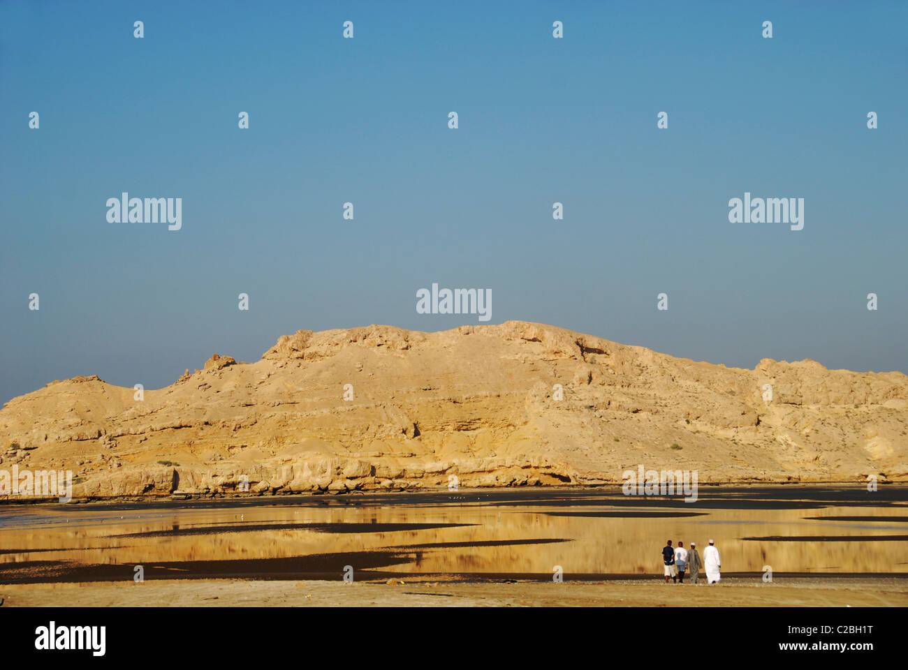 Oman, Sawadi, view of four people walking towards hilly island by lake ...