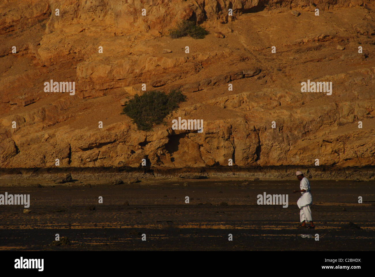 Oman, Sawadi, view of a man in traditional dress walking on a wet ...