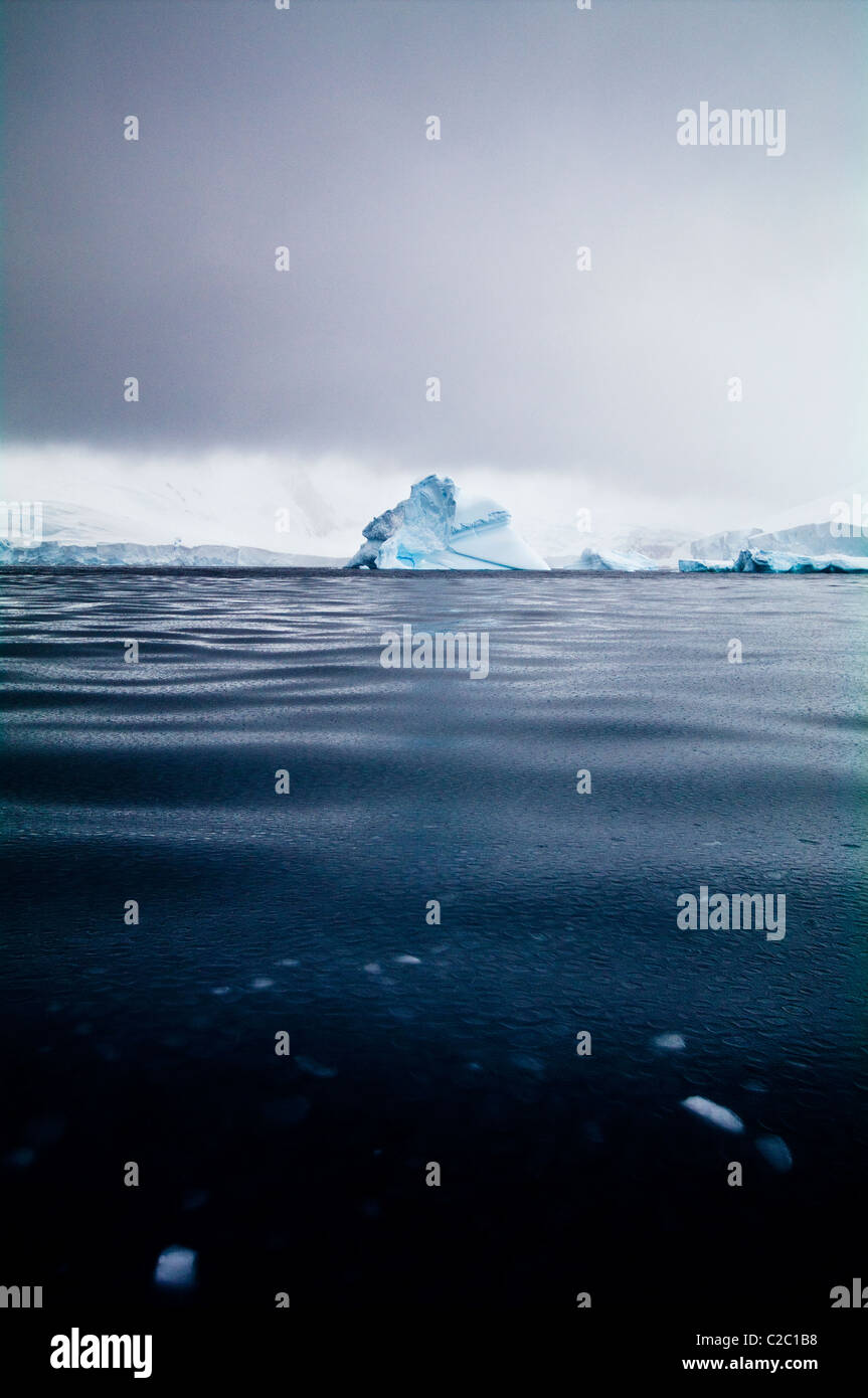 Under stormy skies an iceberg floats through mercury-like Frizzle Ice ...