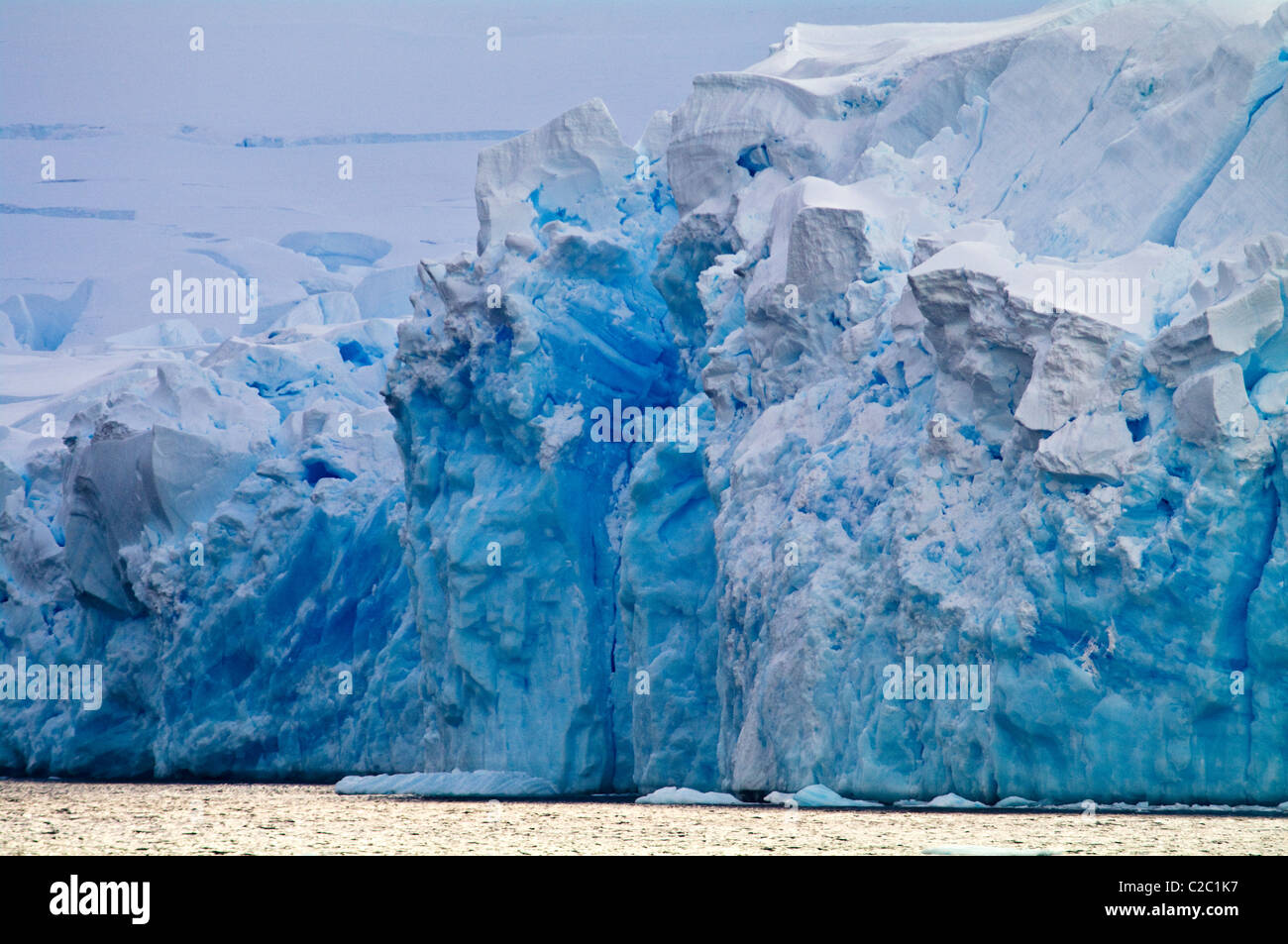 A glaciers jagged and rugged ice cliff towers over the ocean Stock ...