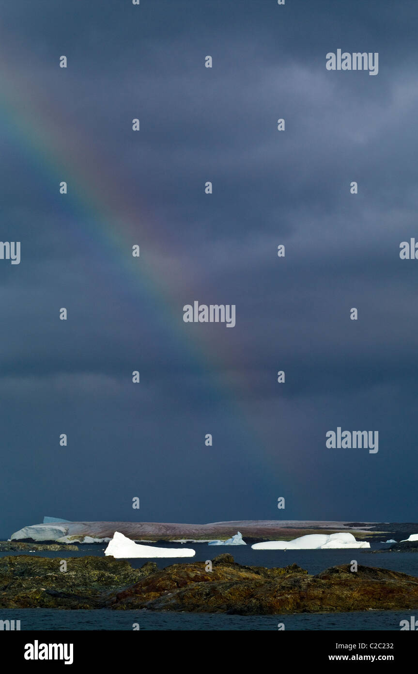 A rainbow descends over icebergs trapped in a rocky bay below a storm ...