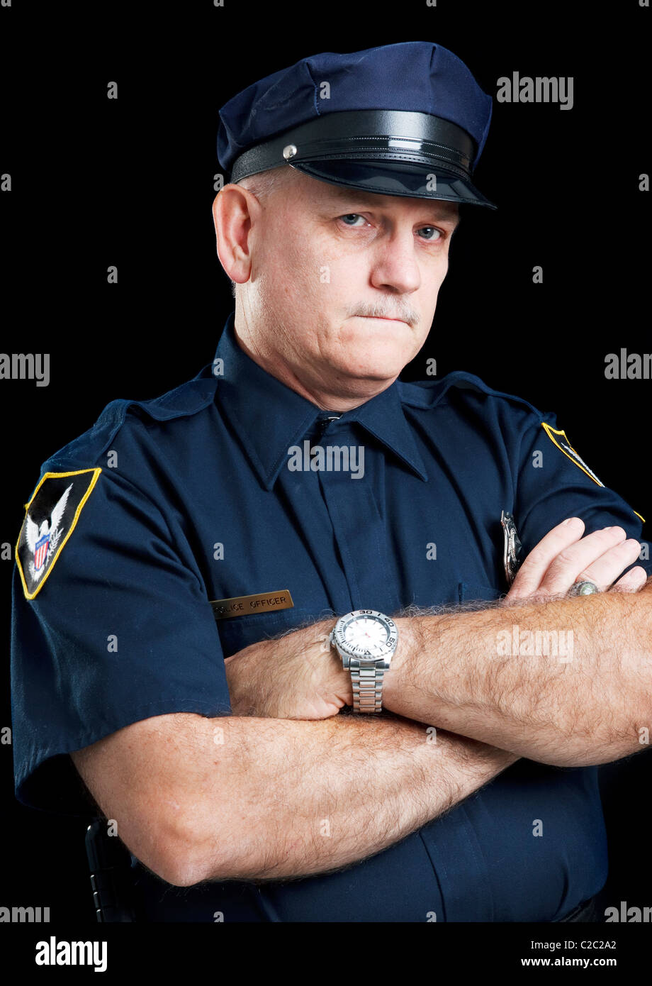 Portrait of a serious police officer with arms folded, against a black ...