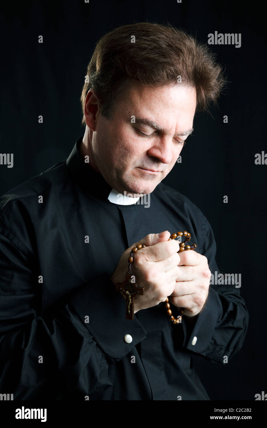 Priest holding his rosary and praying. Black background and dramatic ...