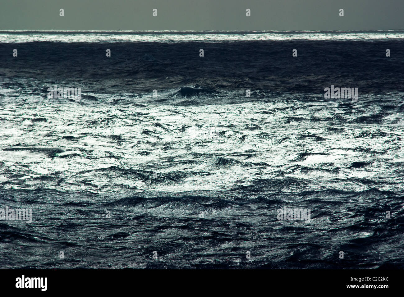 Sunbeams pierce a grey clouds on a stormy featureless ocean horizon ...