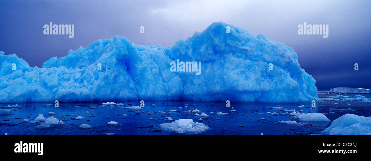 A jagged iridescent blue iceberg rises from a moody calm ocean Stock ...