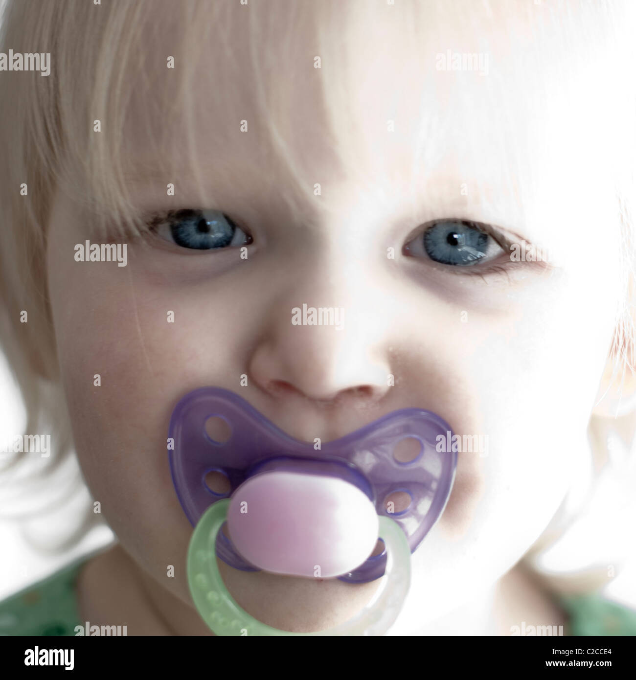 A fair haired and skinned one year old girl with a soother. She appears ...