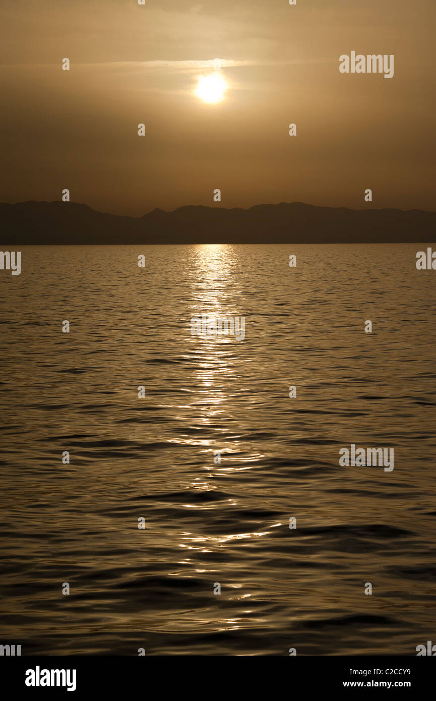 Sunset over water with a reflection and mountains in the distance Stock ...