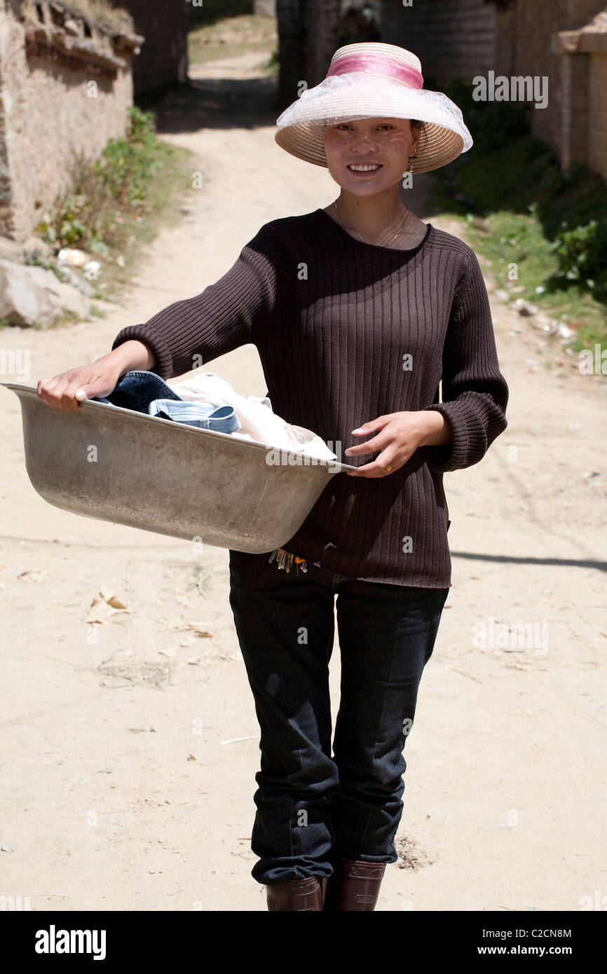 A young woman in a fancy hat carries her washing to the nearest river ...