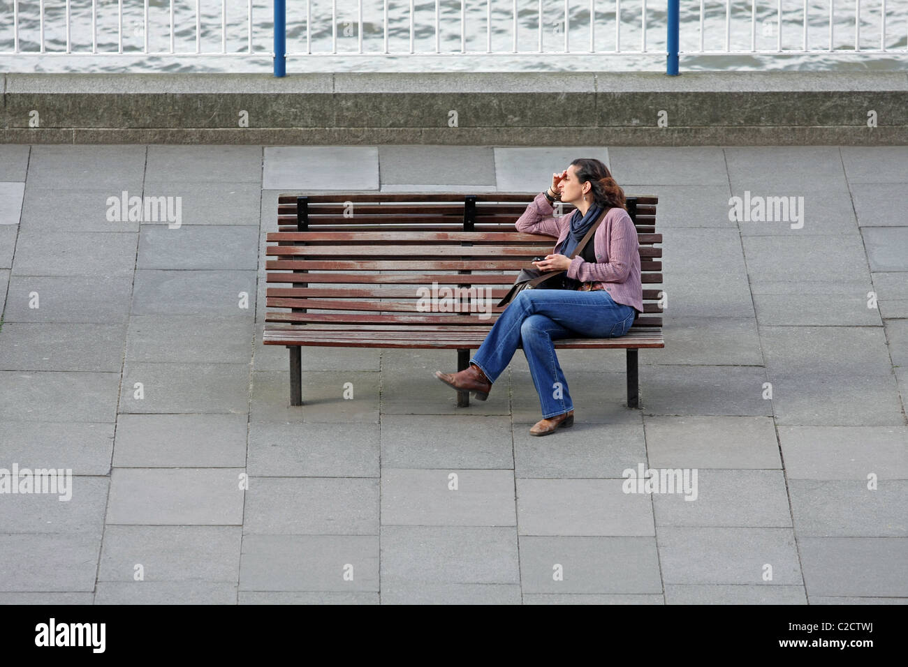 A woman sitting contemplating on a bench on the embankment to the River ...