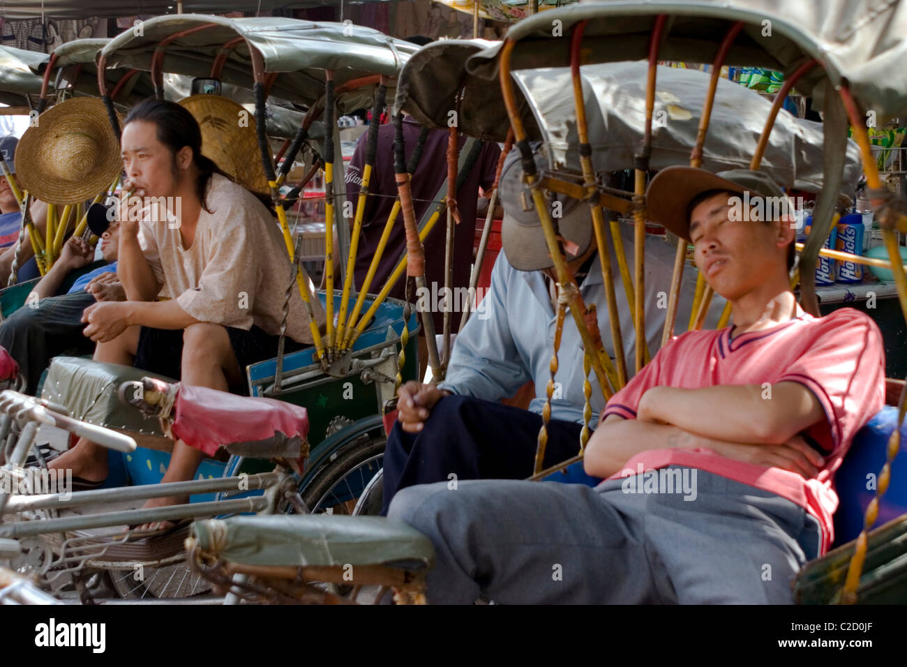A group of male rickshaw drivers are relaxing at a taxi stand in ...