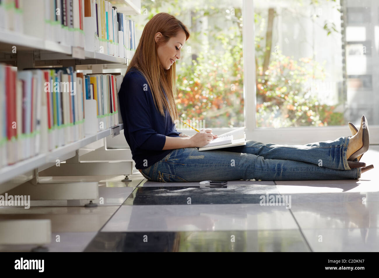 female college student sitting on floor in library, reading book and ...