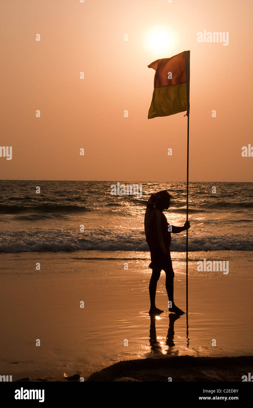 Indian Lifeguard takes out safety flag at sunset at North Goa Stock ...